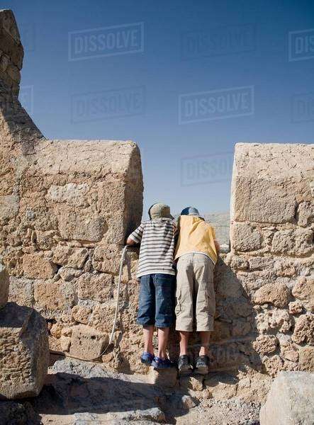 Two boys looking over wall at view - Stock Photo - Dissolve