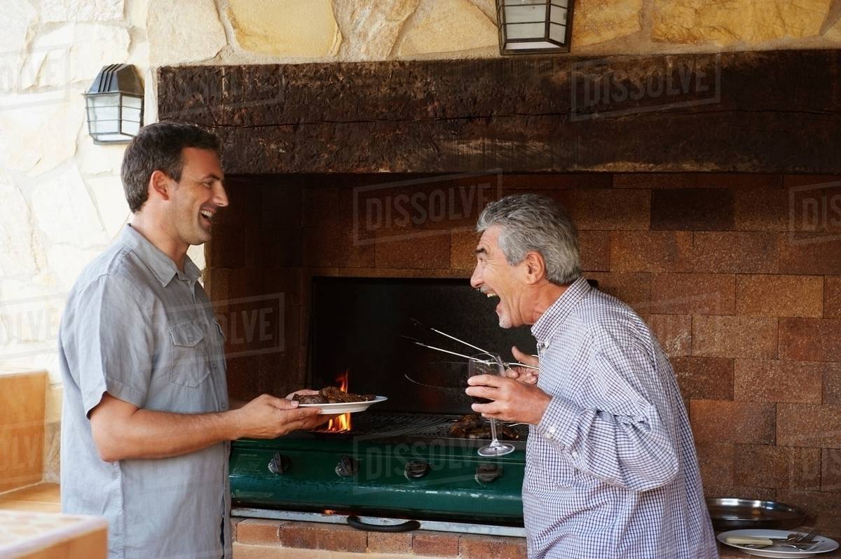 Two men laughing together by barbeque - Stock Photo - Dissolve