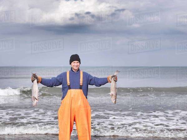 Fisherman on shore holding fish - Stock Photo - Dissolve