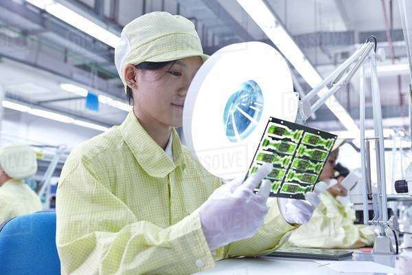 Female worker using magnifying glass at quality check station for a ...