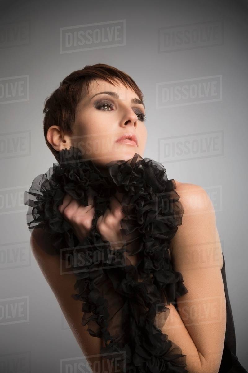 Studio portrait of woman wearing and holding onto black boa ruffle ...