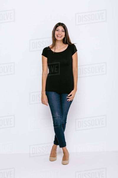 Full length front view of young woman standing legs crossed looking at ...