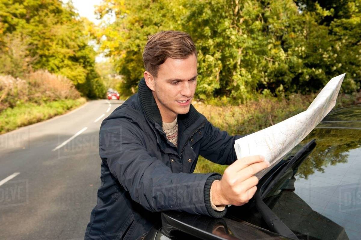 Young man reading map on rural road - Royalty-free Stock Photo | Dissolve