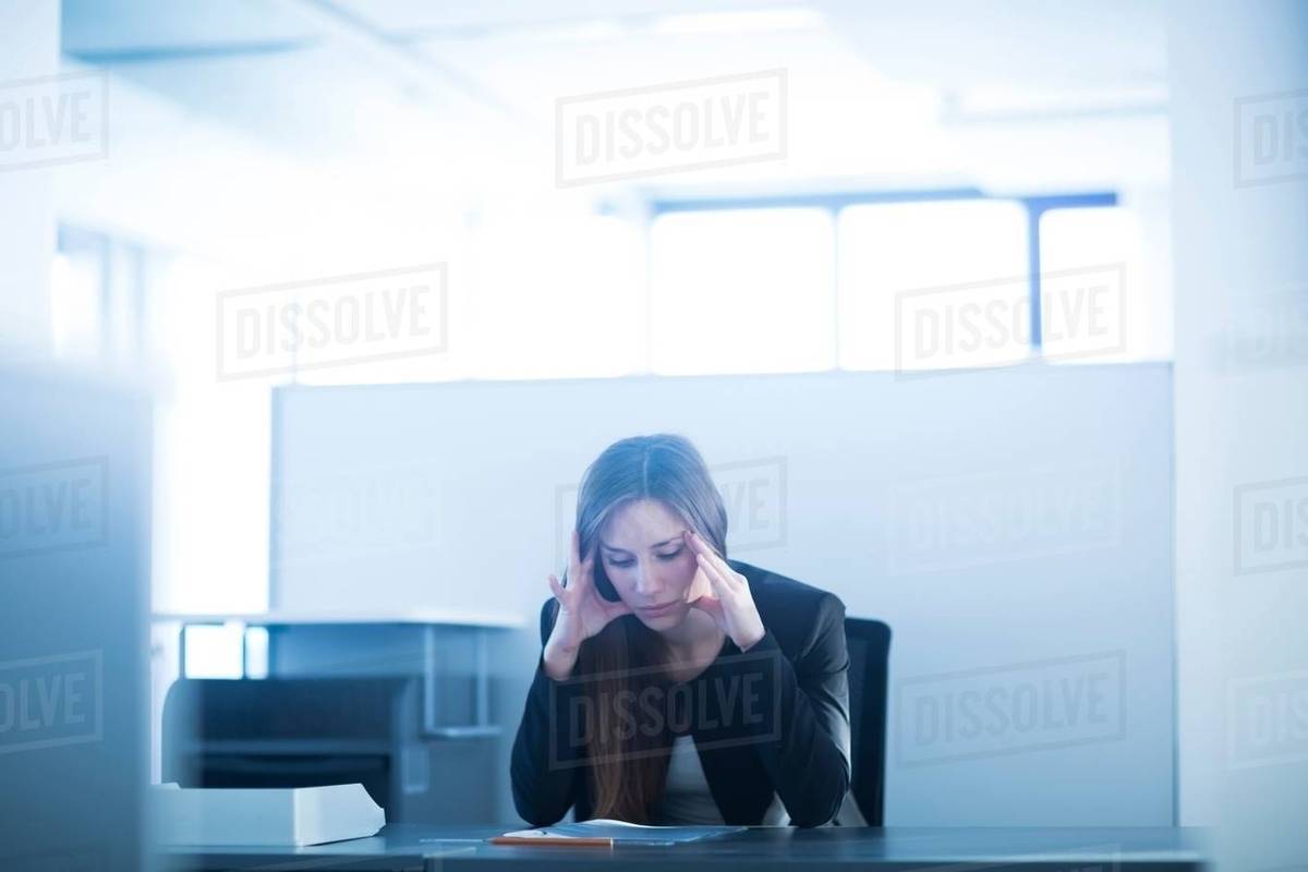 Young woman sitting at desk in office, head in hands looking down ...