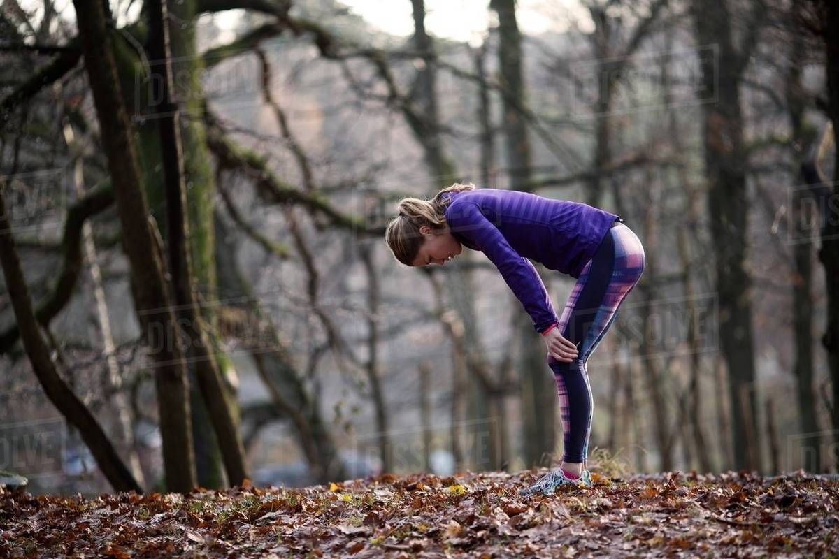 Side view of young woman wearing sports clothing bending over hands on ...