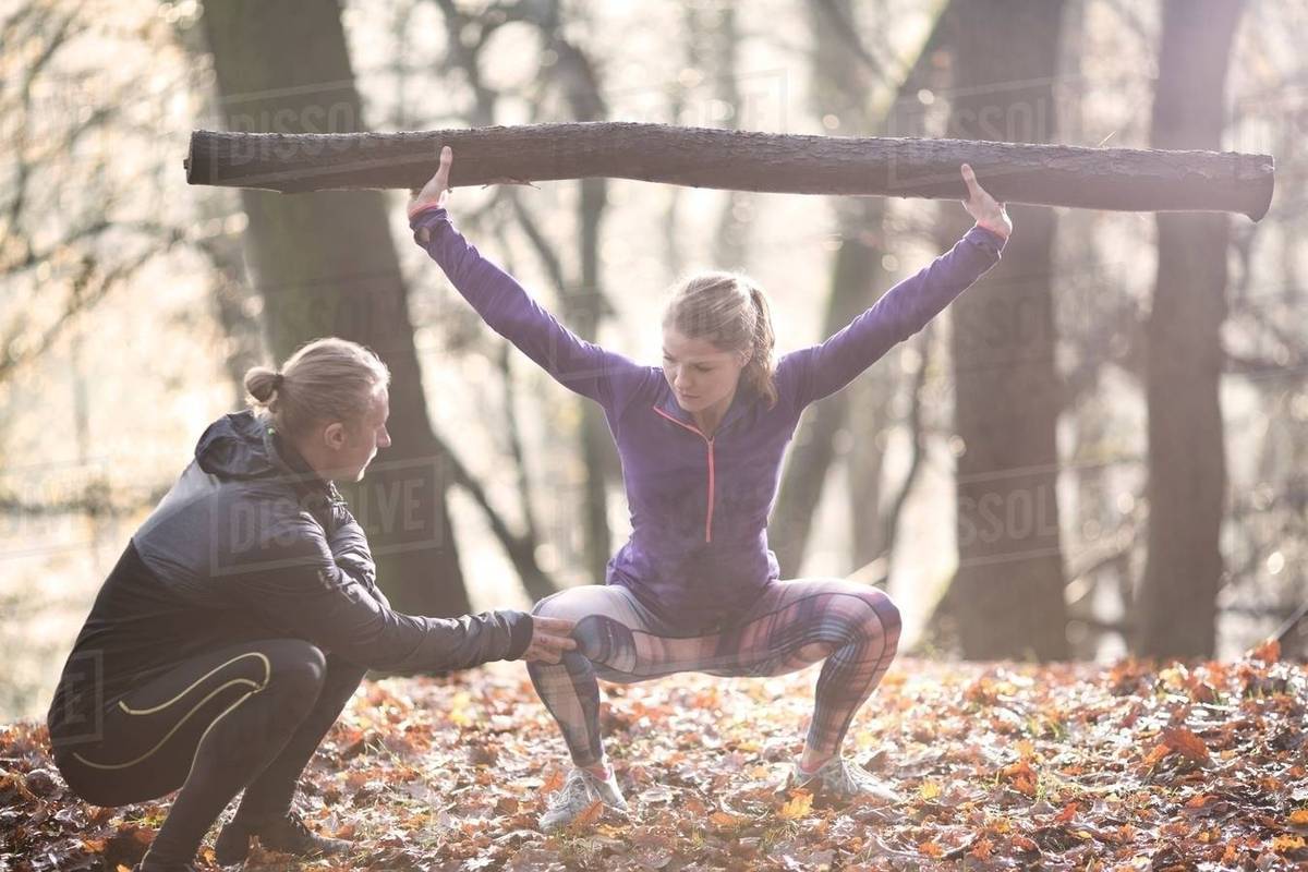 Young woman squatting in forest, arms raised holding tree branch ...