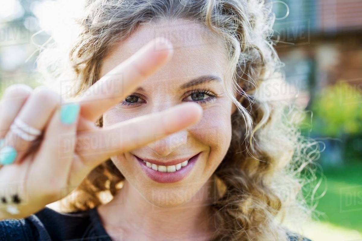 Young woman making peace sign with hand - Stock Photo - Dissolve