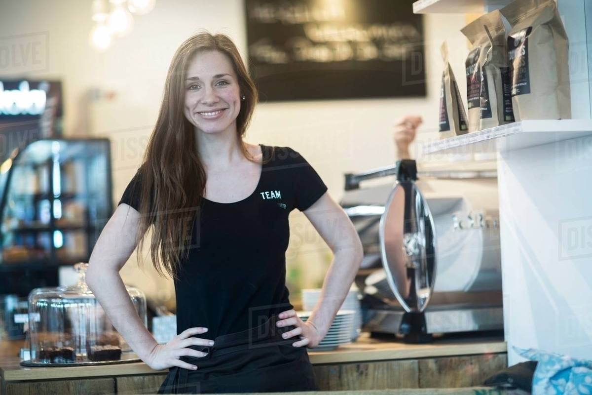 Portrait of young female waitress behind kitchen counter in cafe ...