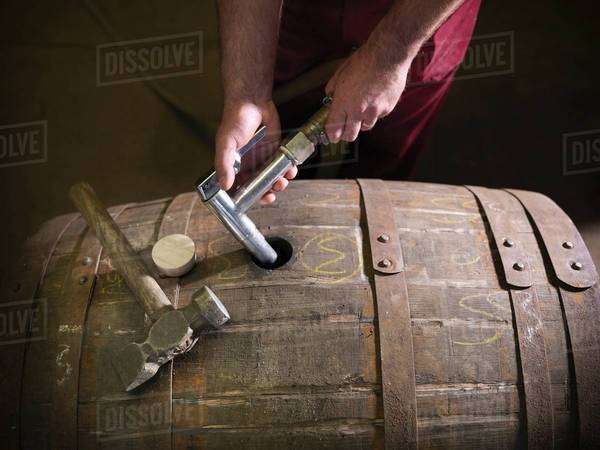 Worker filling whisky barrel in distillery - Stock Photo - Dissolve