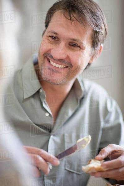Smiling man buttering bread - Stock Photo - Dissolve