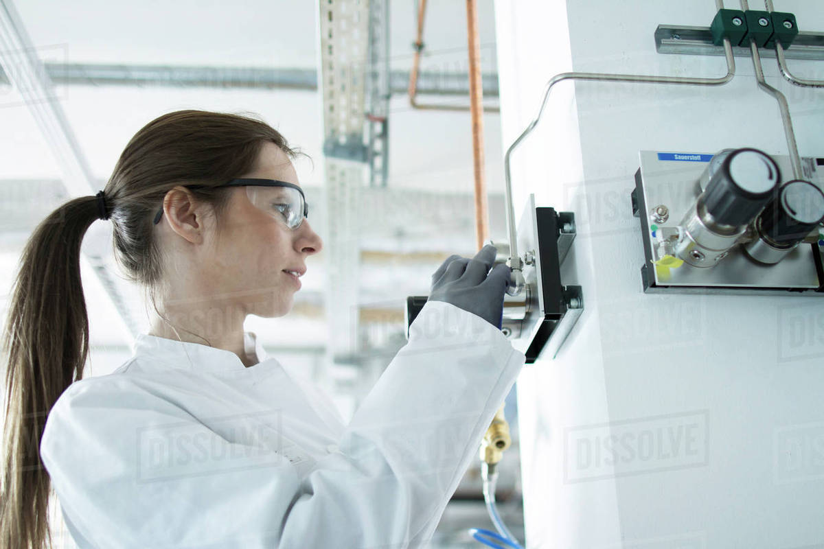 Side view of woman in workshop wearing safety goggles and coat ...