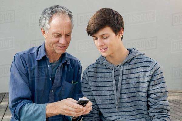 Father and son using cell phone together - Stock Photo - Dissolve