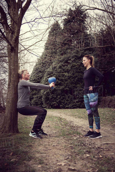 Side view of woman crouching against tree holding kettle bell - Royalty ...