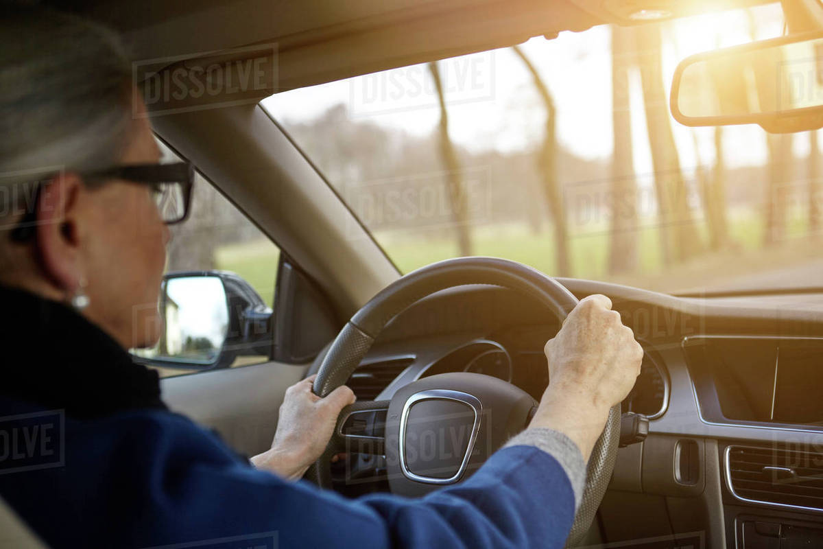 Over the shoulder view of woman in car driving on tree lined road ...