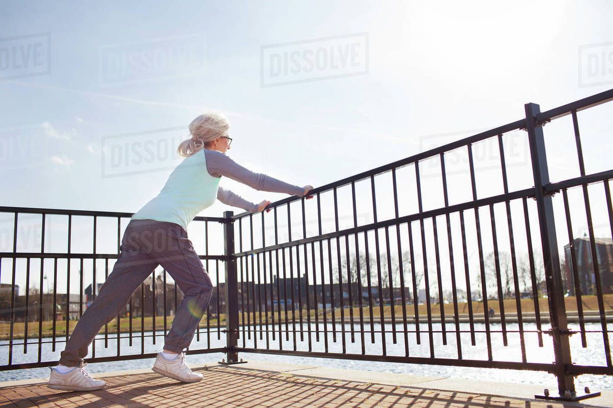 Full length side view of woman leaning against railing stretching ...