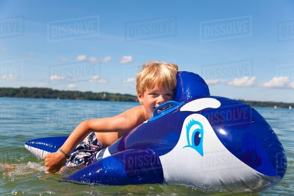 Boy floating in lake with toy whale - Stock Photo - Dissolve