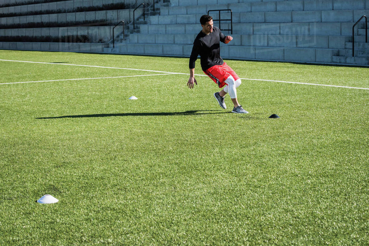 Young man running doing agility training with markers on playing field ...