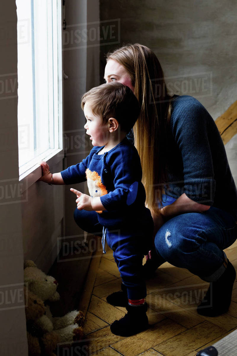 Mid adult woman and baby son looking through living room window - Stock ...