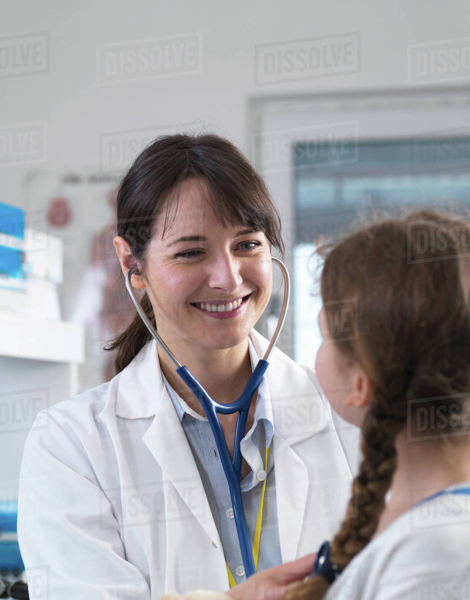 Female paediatric doctor listening to a young girl's chest with a ...
