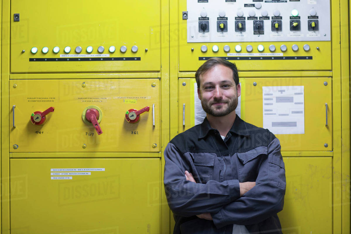 Man in front of yellow control panel, arms crossed smiling - Stock ...
