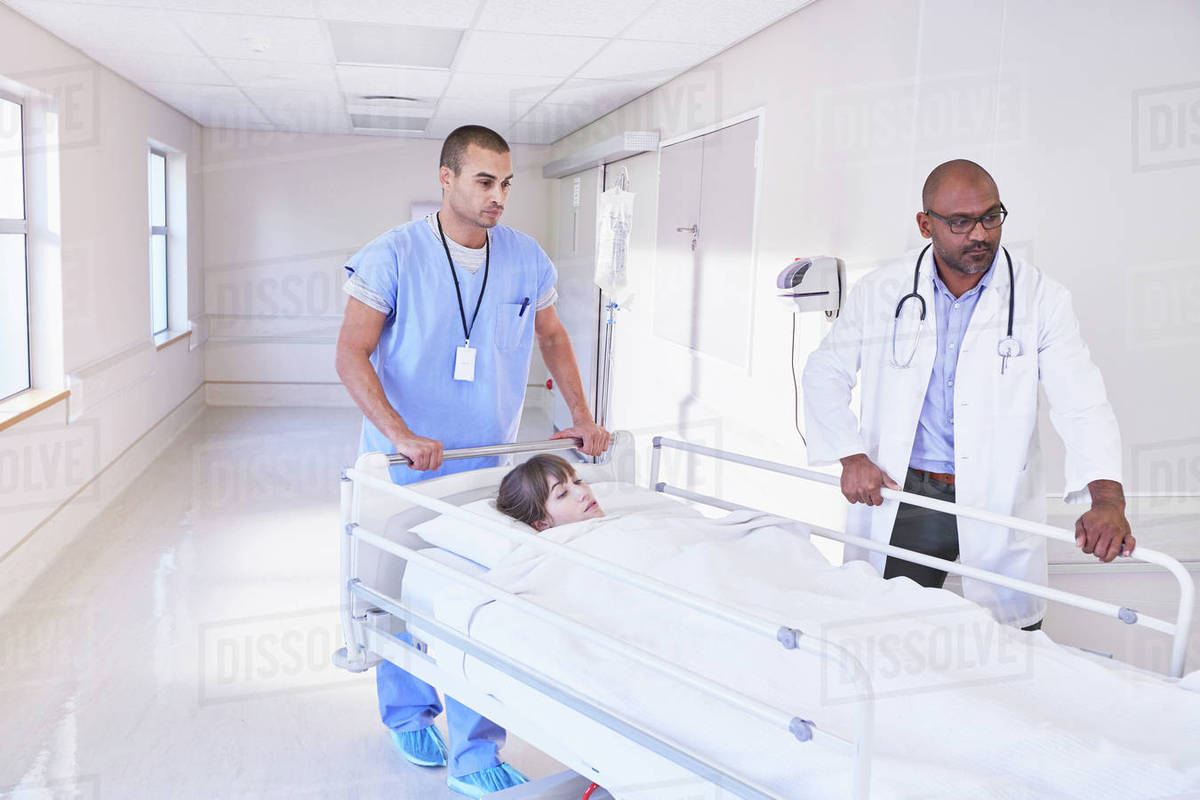 Doctors pushing patient in hospital bed through corridor - Royalty-free ...