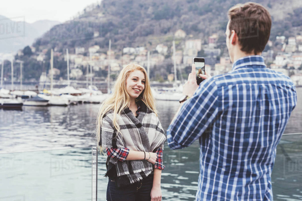 Young man on waterfront photographing girlfriend, Lake Como, Italy ...