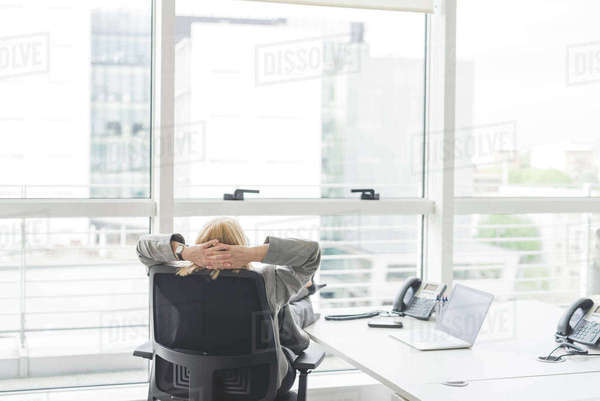 Rear view of businesswoman sitting on office desk chair looking out of ...