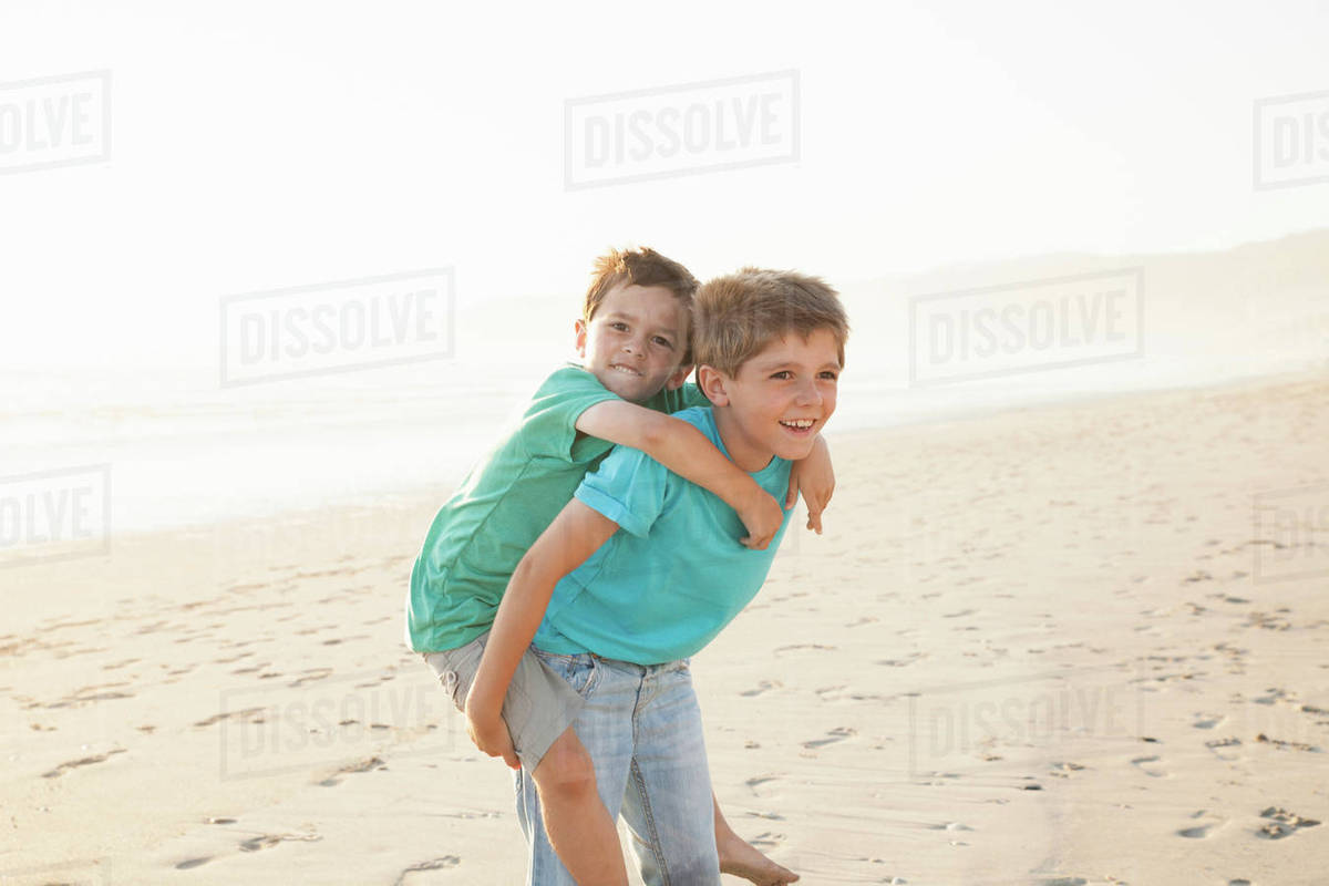 Boy giving brother piggyback on beach - Stock Photo - Dissolve