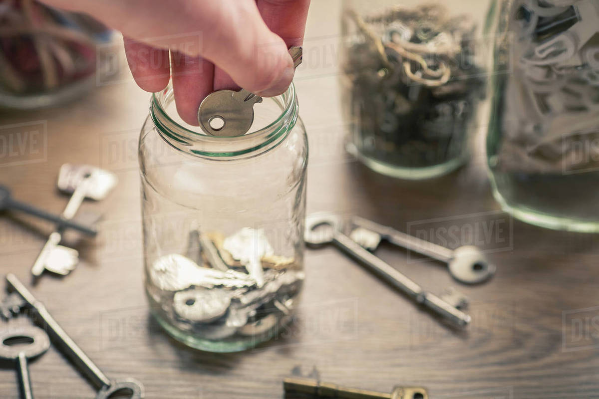 Man's hand putting keys in jar - Stock Photo - Dissolve