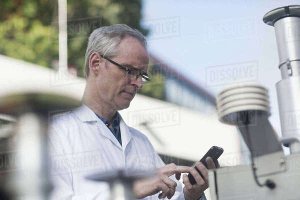 Male meteorologist texting on smartphone at outdoor weather station ...