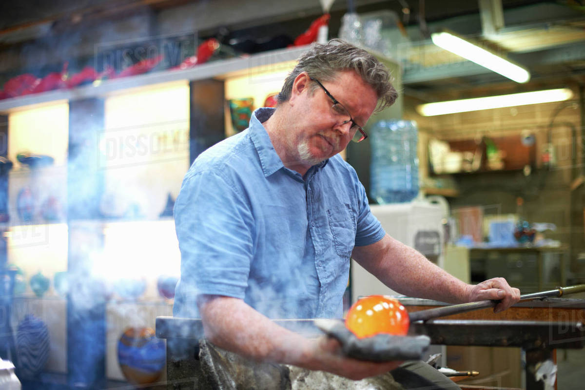 Glassblower in workshop forming molten glass on blowpipe - Royalty-free ...