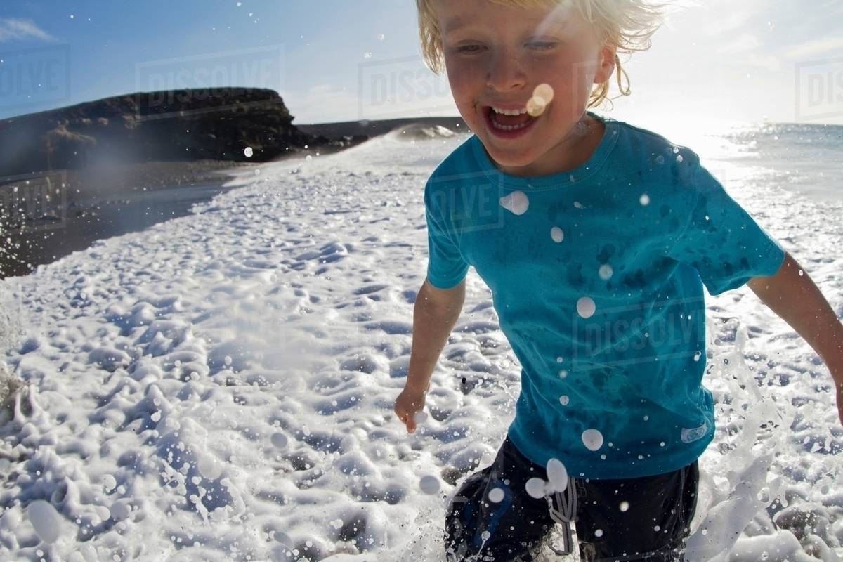 Boy playing in waves on beach - Stock Photo - Dissolve
