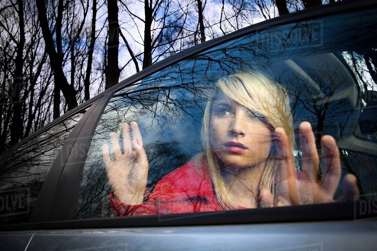 Woman peering out car window in woods - Stock Photo - Dissolve