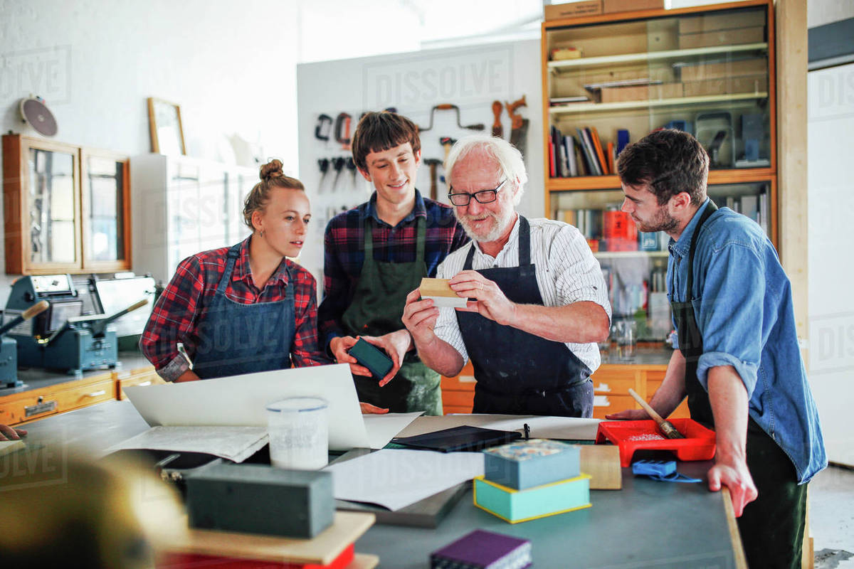Senior male workshop leader showing materials to young group of men and ...