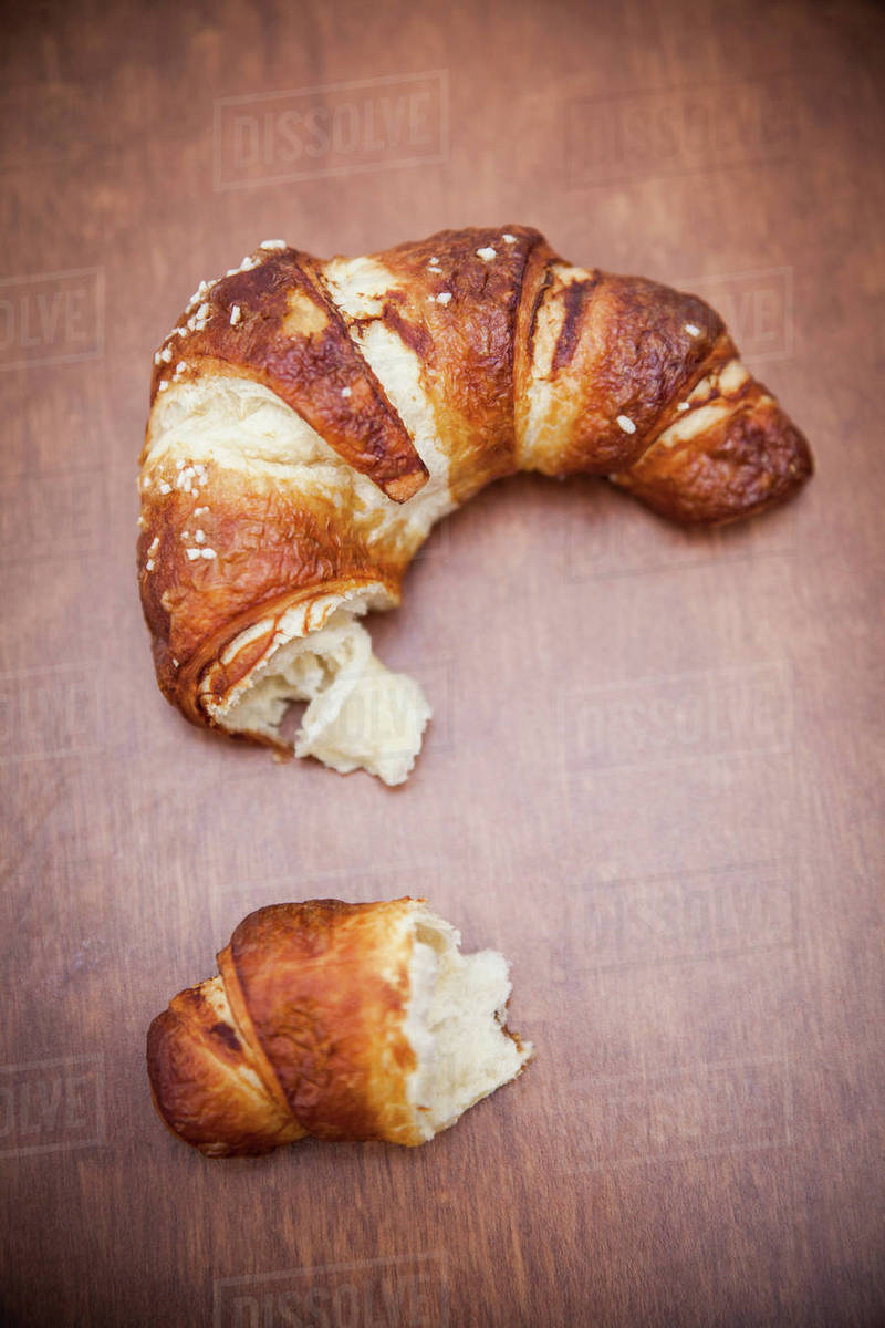 Broken croissant on wooden table - Stock Photo - Dissolve