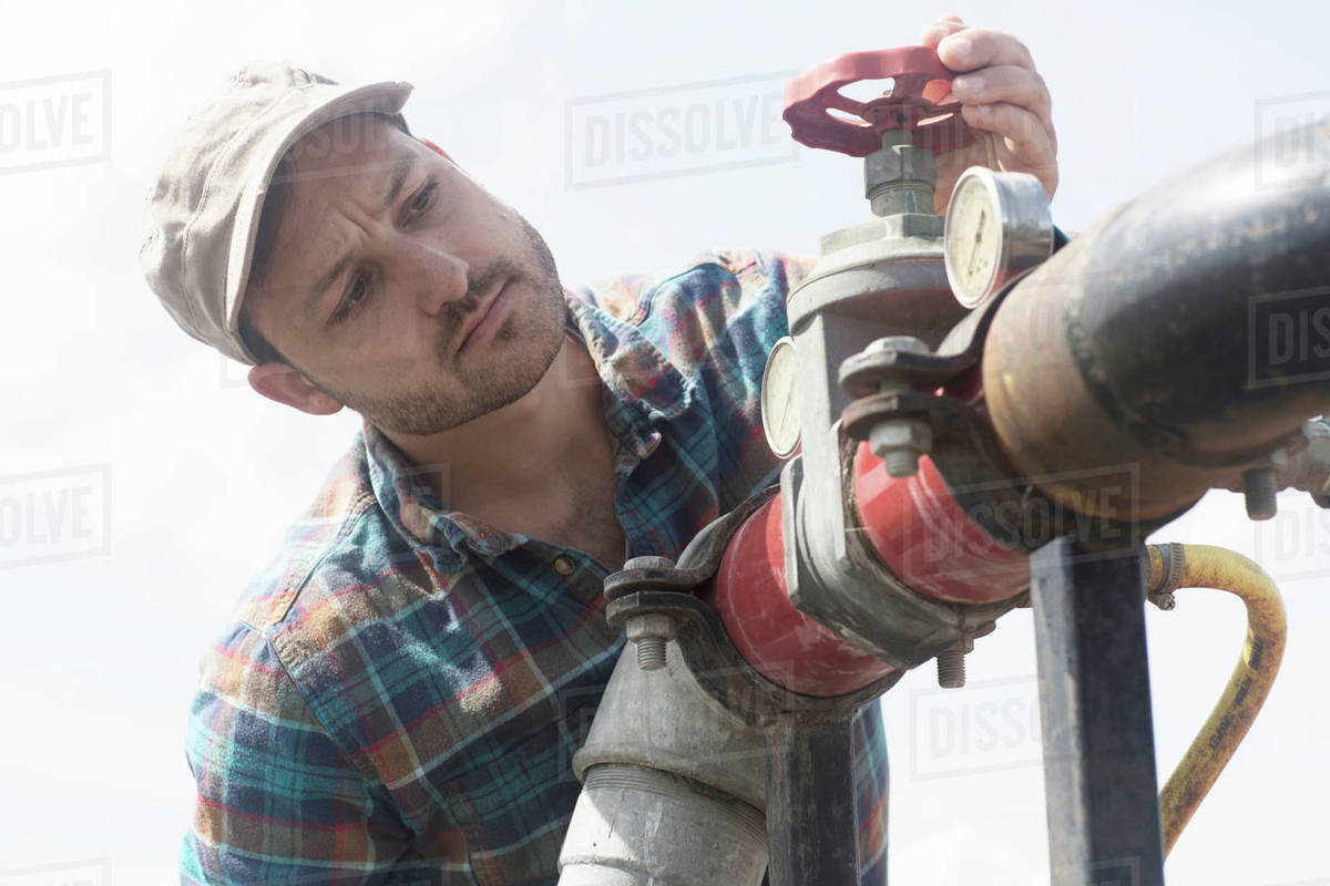 Man opening valve on industrial piping - Stock Photo - Dissolve