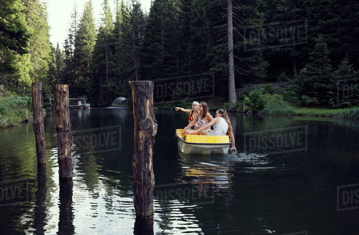 Three adult female friends pointing from rowing boat on lake ...