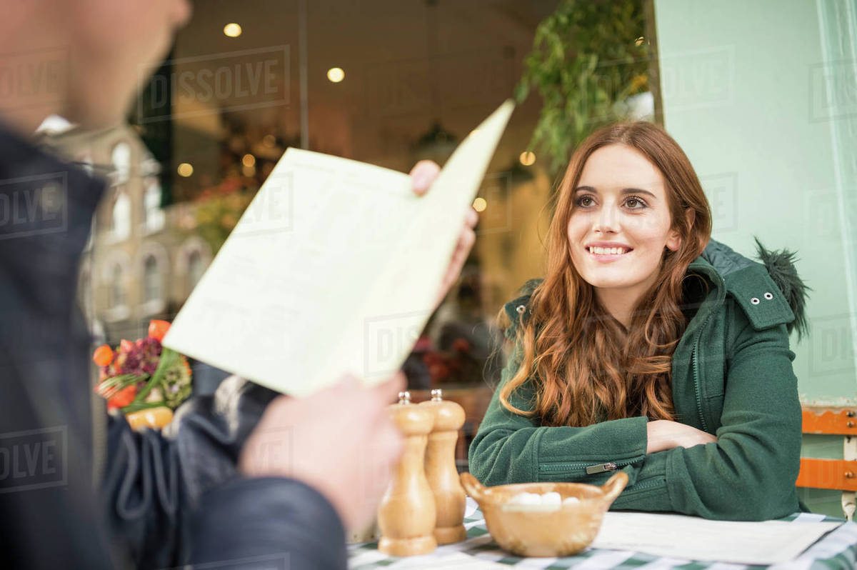 Couple at pavement cafe looking at menu smiling - Stock Photo - Dissolve