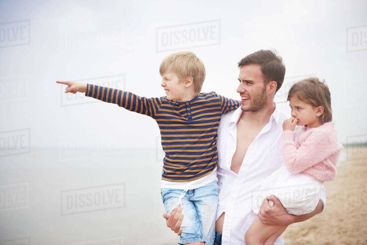 Father carrying children in arms on beach - Stock Photo - Dissolve