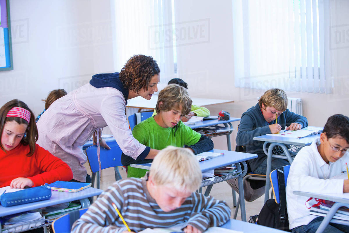 Teacher helping boy with problem in classroom - Stock Photo - Dissolve