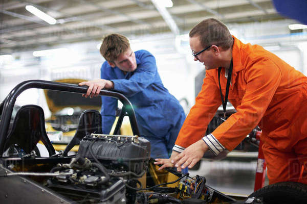 College mechanic students discussing racing car engine in repair garage ...
