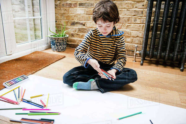 Boy sitting on floor drawing on long paper - Stock Photo - Dissolve