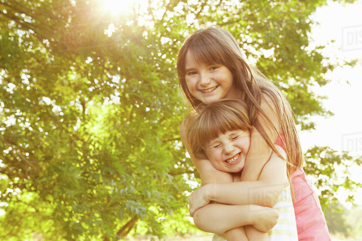 Portrait of girl being hugged by big sister in park - Royalty-free ...
