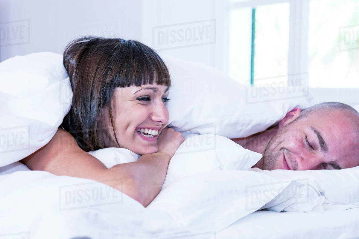 Couple laughing under duvet on bed - Stock Photo - Dissolve