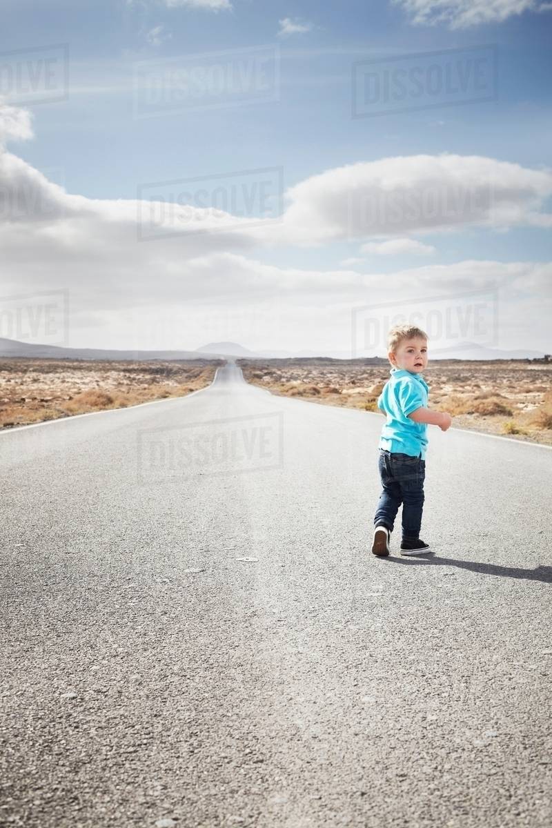 Boy walking on paved rural road - Stock Photo - Dissolve