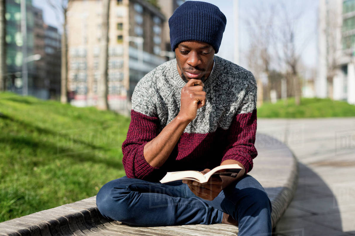 Man sitting on bench, reading book, thoughtful expression - Royalty ...