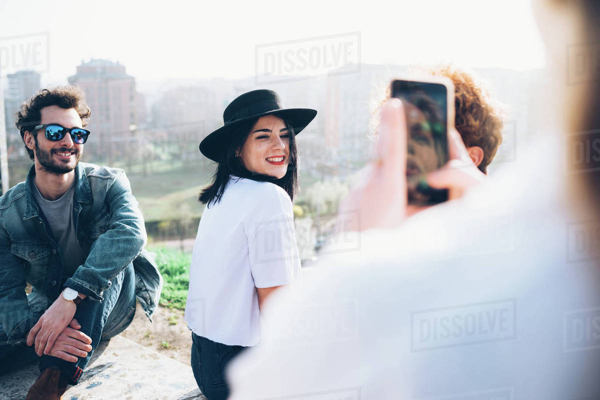 Group of friends enjoying roof party, young woman photographing friends ...
