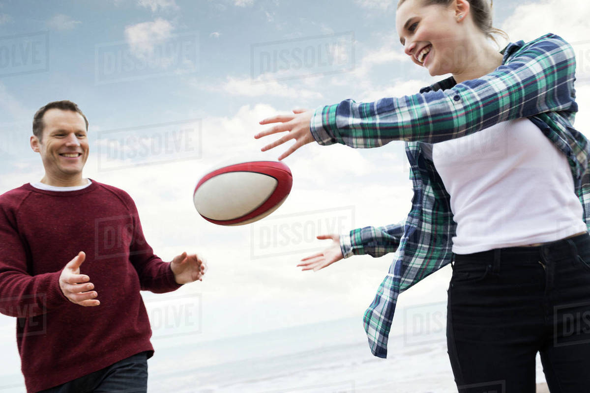 Father and daughter playing rugby on beach - Stock Photo - Dissolve
