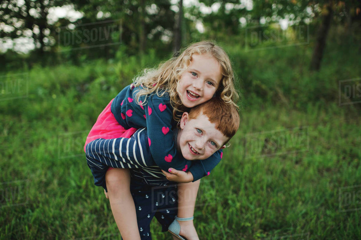 Portrait of boy giving sister a piggyback in field - Stock Photo - Dissolve