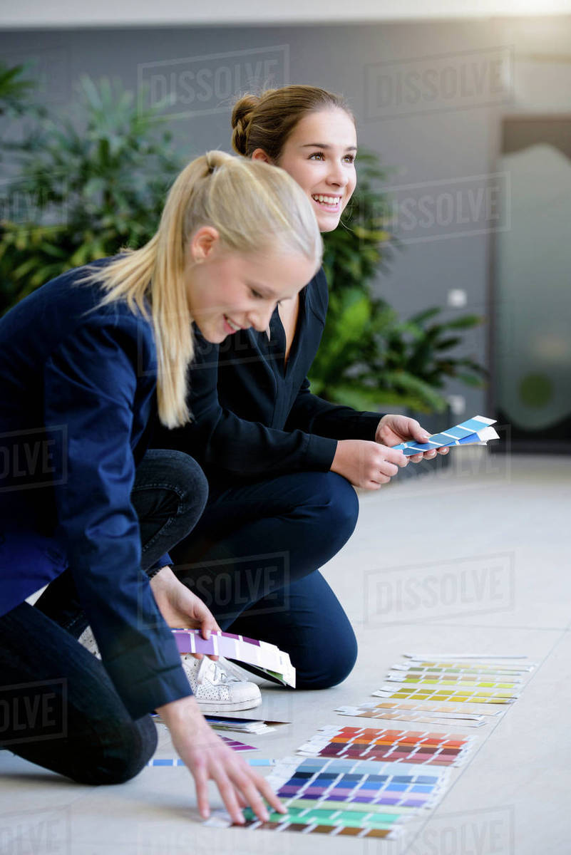 Two young businesswomen crouching on office floor looking at colour ...